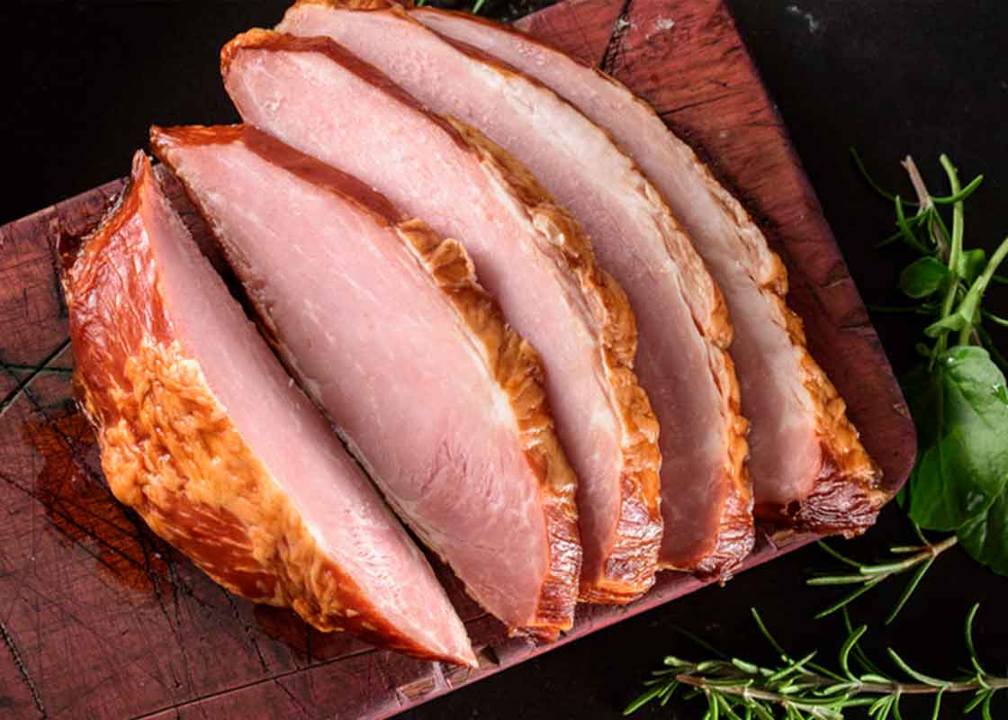 Image is of a sliced glazed ham sitting on a cutting board