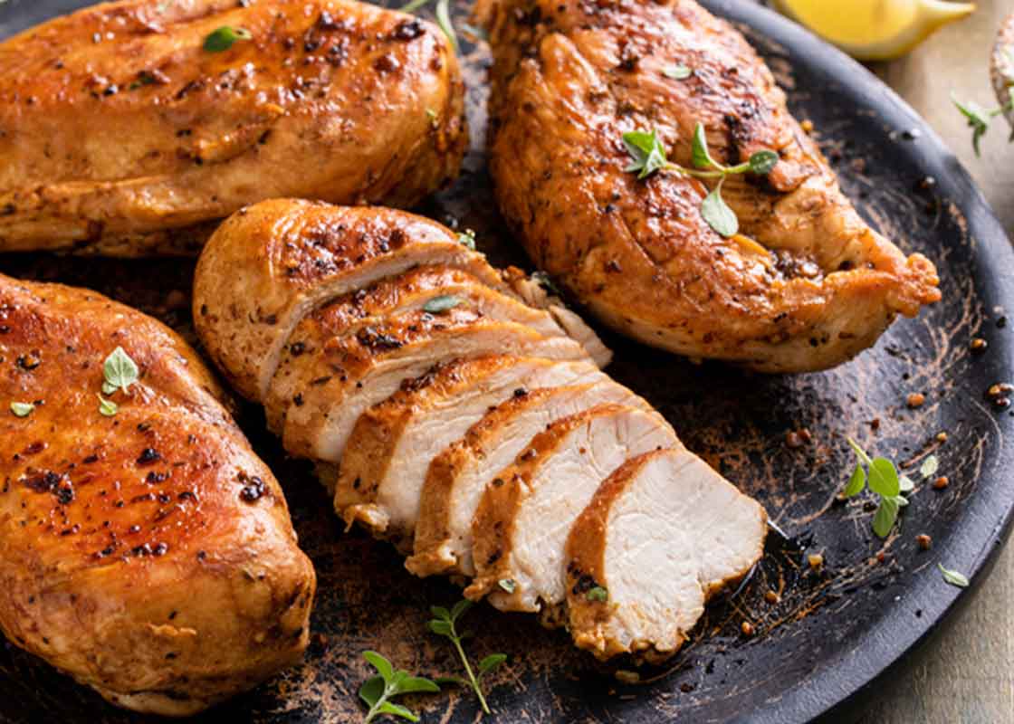 Image is of four grilled chicken breast and one is sliced on a plate