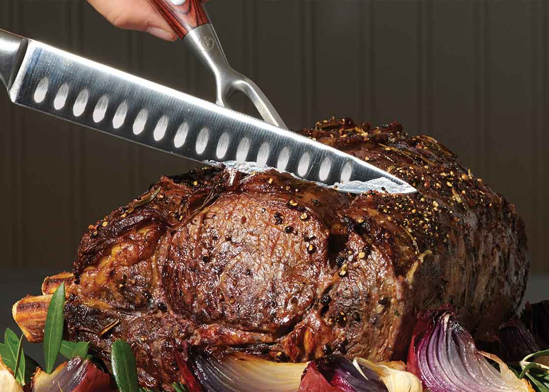 Image is of someone carving ad fully prepared Prime Rib with a knife ...