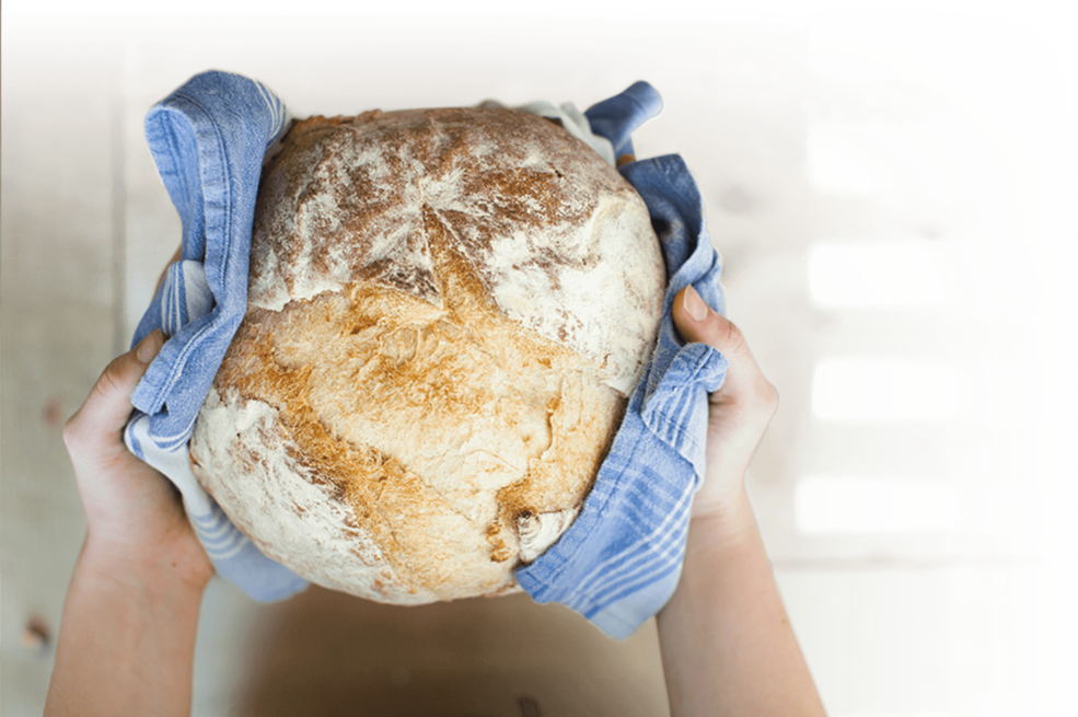 Two hands holding a loaf of freshly baked bread.