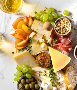 A variety of different cheeses surrounded by fruit and olives ...